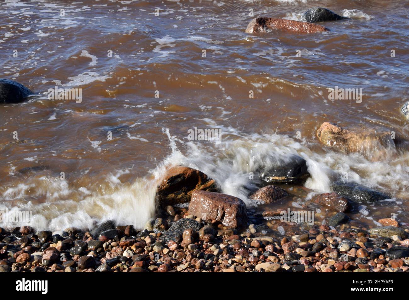 Colored pebbles at the shoreline with water and waves Stock Photo - Alamy