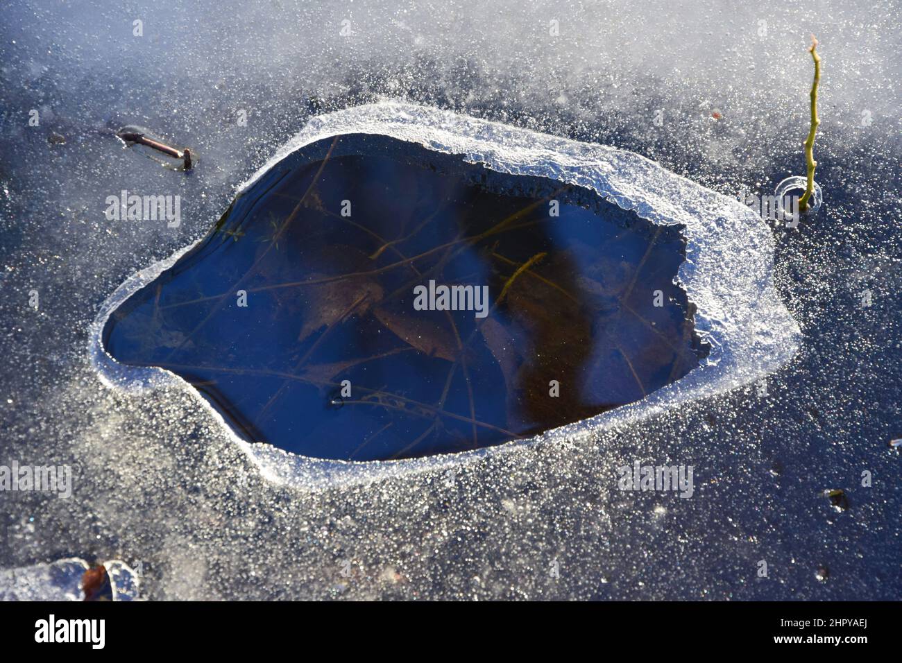 Closeup of a small hole cracked on the frozen surface of a lake Stock ...