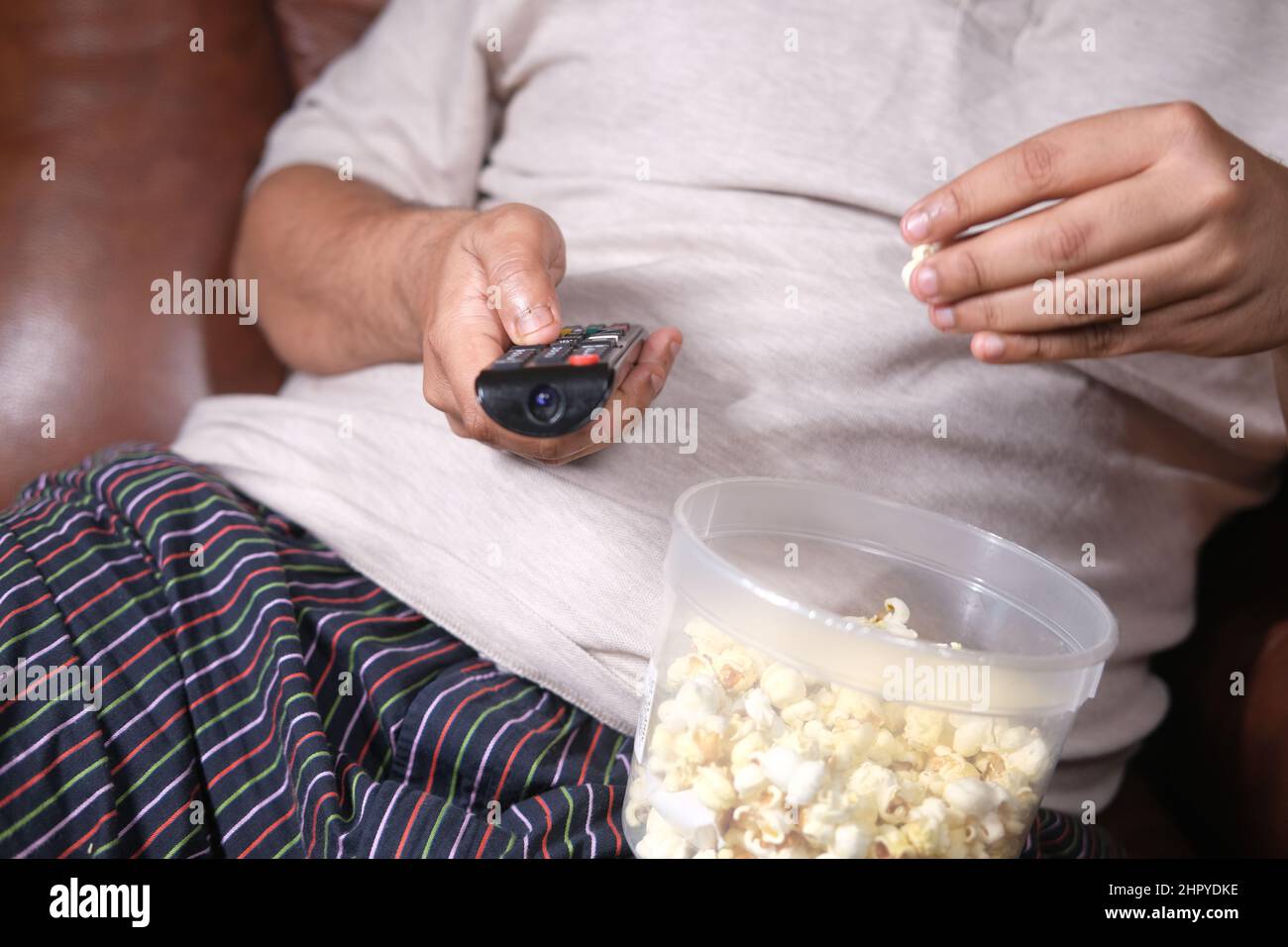 a fat man eating popcorn and holding Tv remote sitting on sofa Stock ...