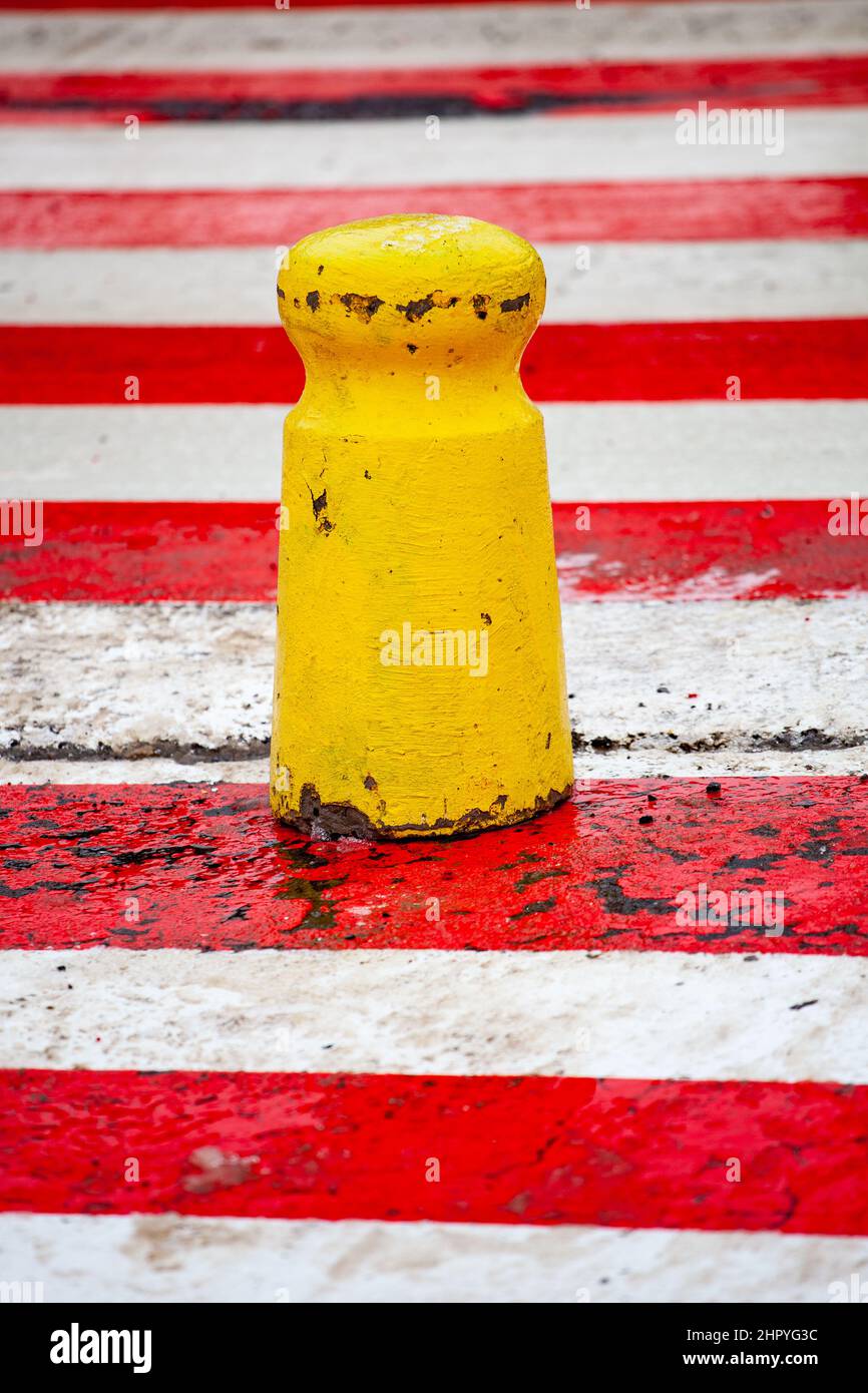 Yellow concrete post on a red and white crosswalk. Parking barrier at ...
