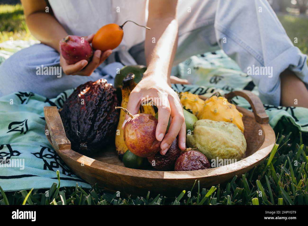 Woman picking fruits with assorted fruits on a wooden plate in a picnic ...