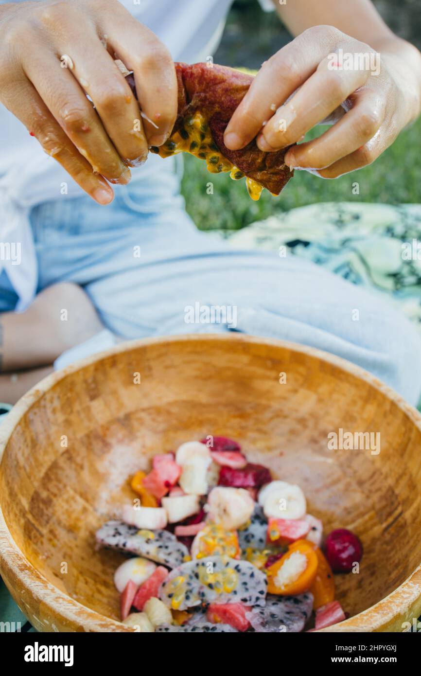 Vertical shot of woman pressing passion fruit into a bowl with assorted ...