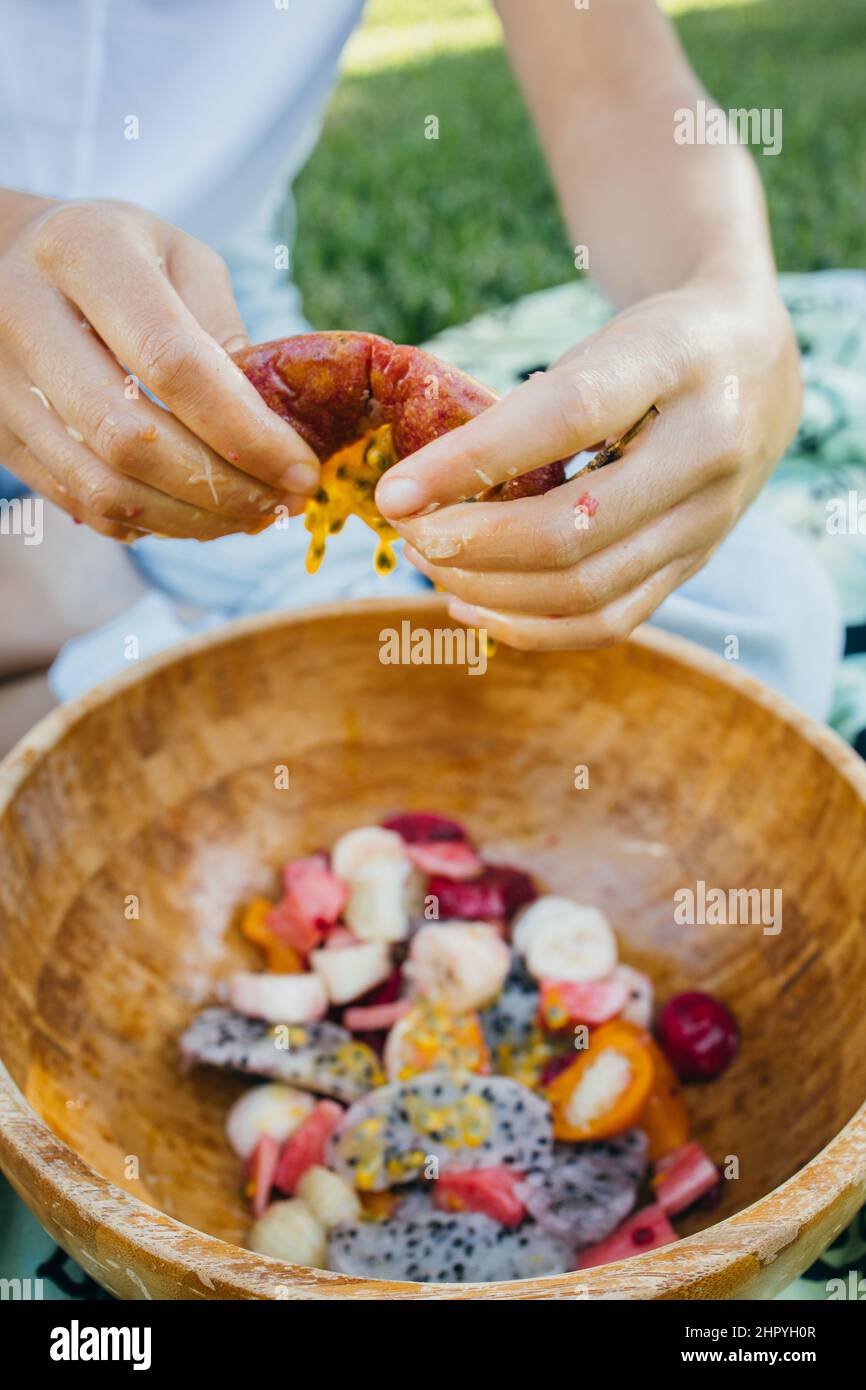 Vertical shot of woman pressing passion fruit into a bowl with assorted ...