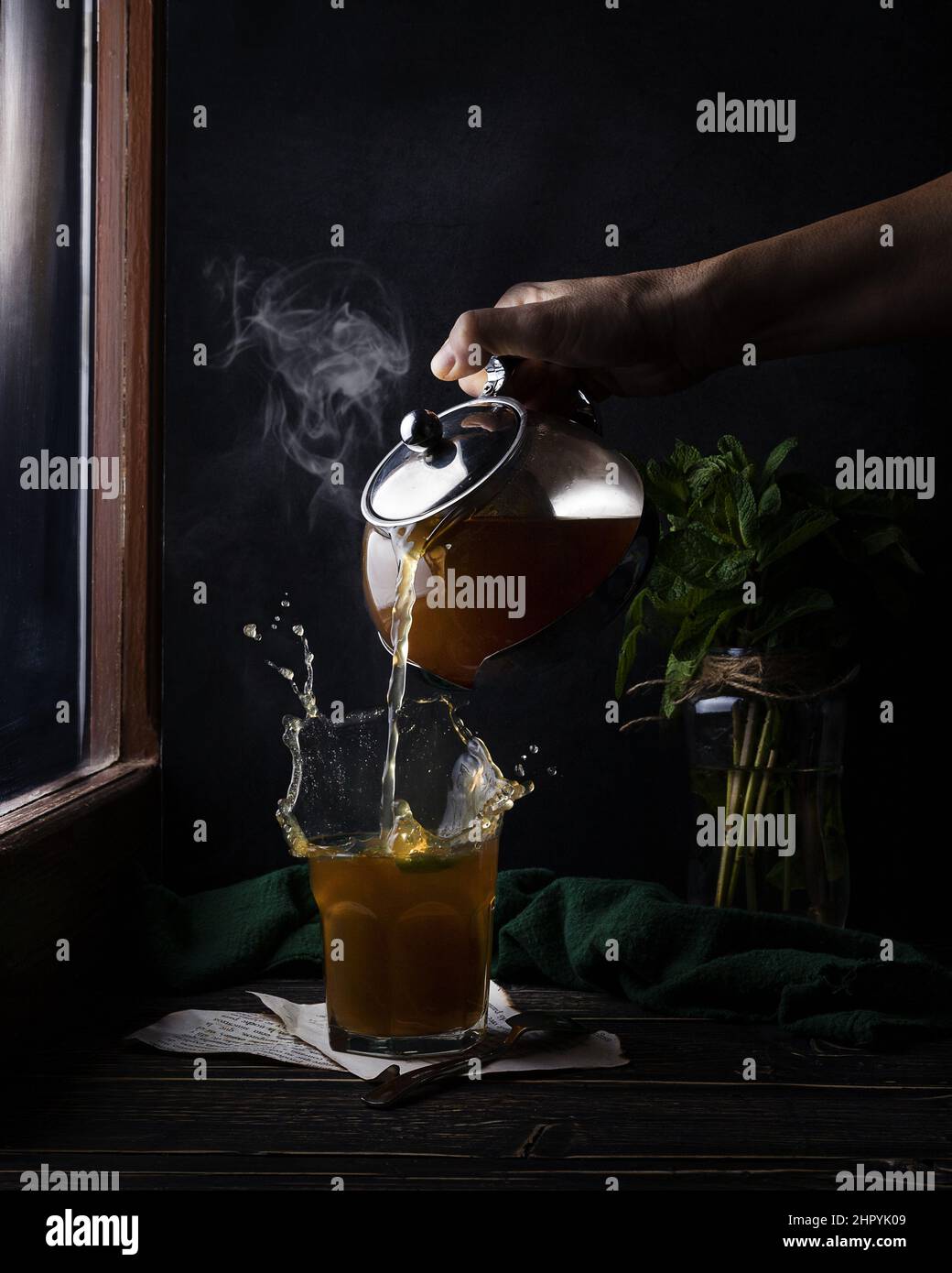 Vertical shot of a person pouring tea from the kettle into the cup ...