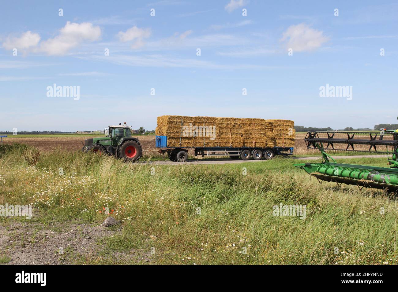 a tractor is driving with a long wagon with straw bales at a road in ...