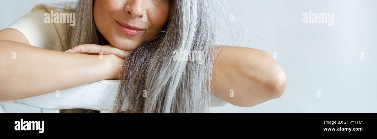 Cheerful middle aged Asian lady with flowing hoary hair sits backwards ...