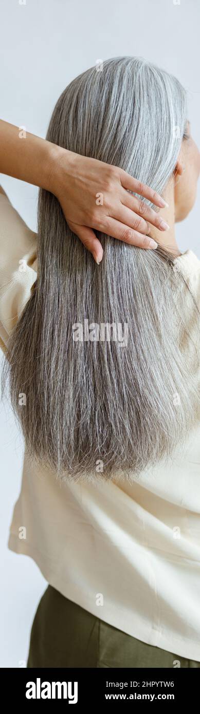 Middle aged woman adjusts long loose hoary hair on light grey ...