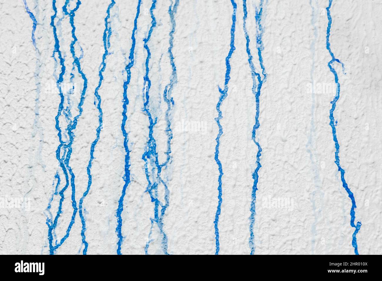Streaks of liquid spilled blue paint down the white plaster wall ...