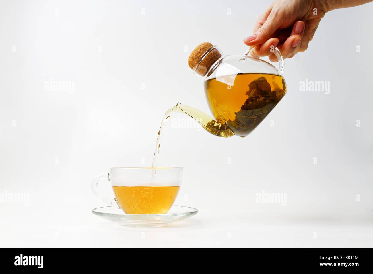 Human hand pours tea from a transparent kettle into a transparent cup ...