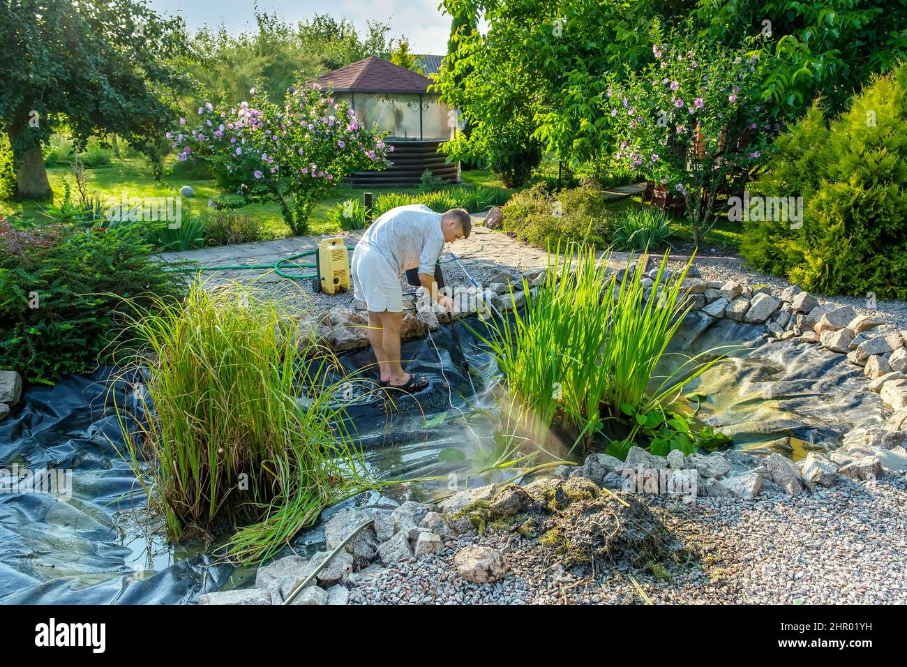man cleans garden pond bottom with high-pressure washer from mud and ...