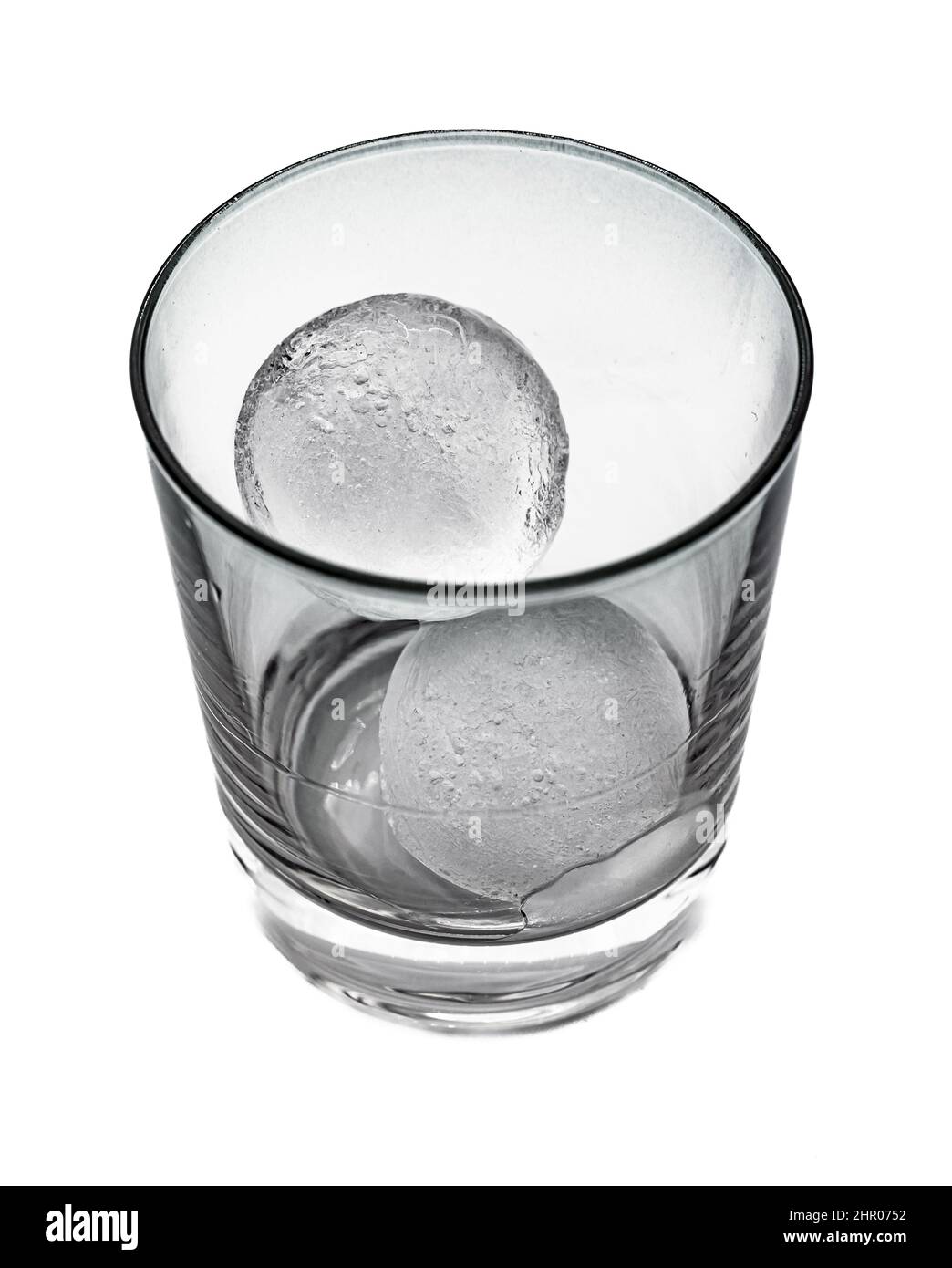 High contrast view of a clear glass with two round ice cubes isolated ...