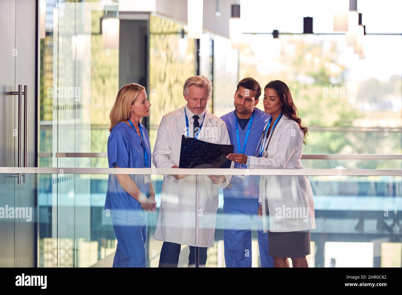 Multi-Cultural Medical Team Wearing White Coats And Scrubs Discuss Patient Scan Meeting In ...