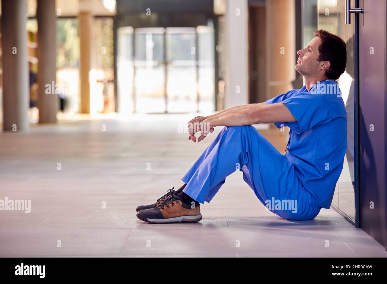 Tired And Overworked Medical Worker In Scrubs Sitting On Floor Of ...