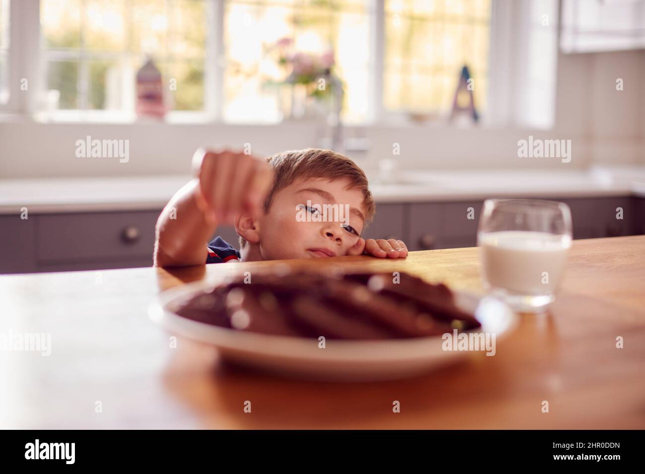 Boy At Home In Kitchen Reaching Up To Take Cookie From Plate On Counter ...