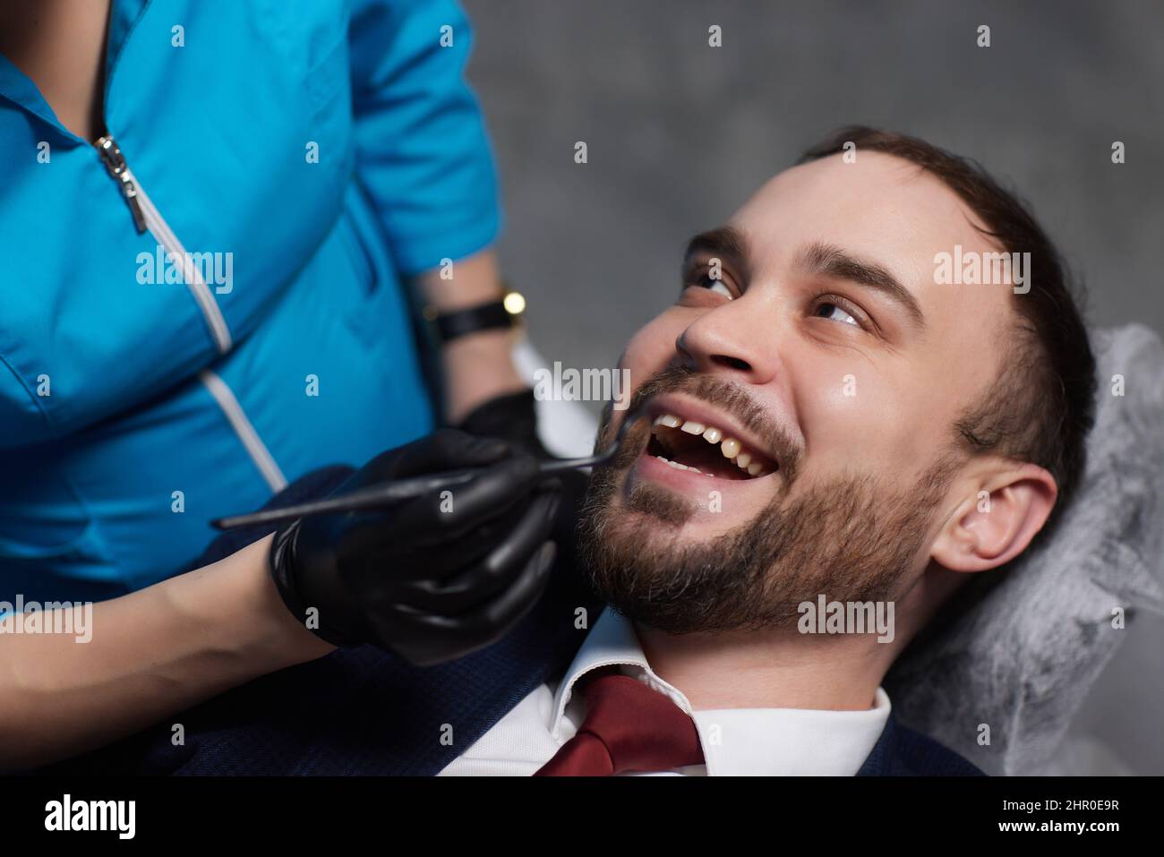 Smiling young man sitting in dentist chair while doctor examining his ...