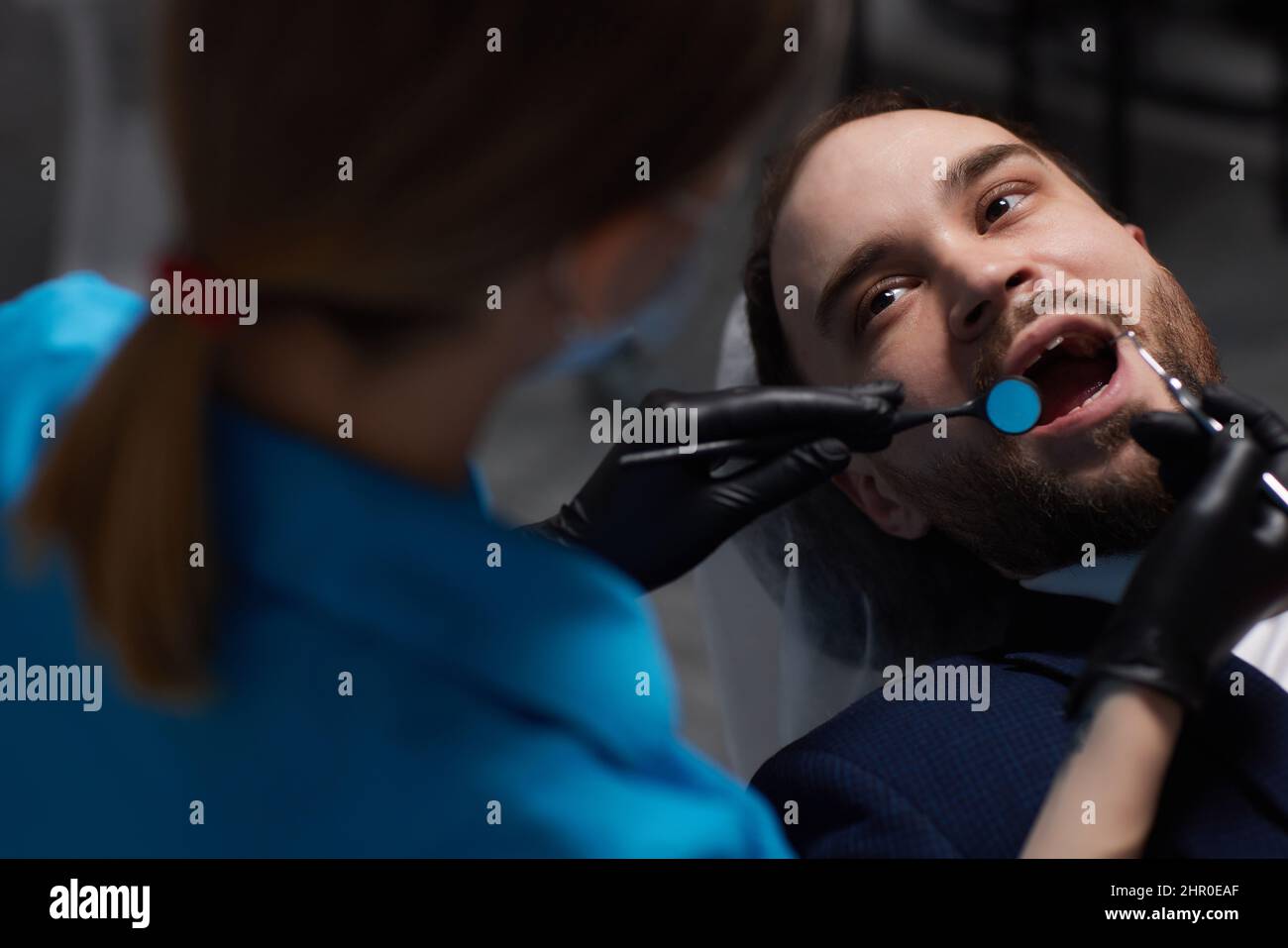 Smiling young man sitting in dentist chair while doctor examining his ...