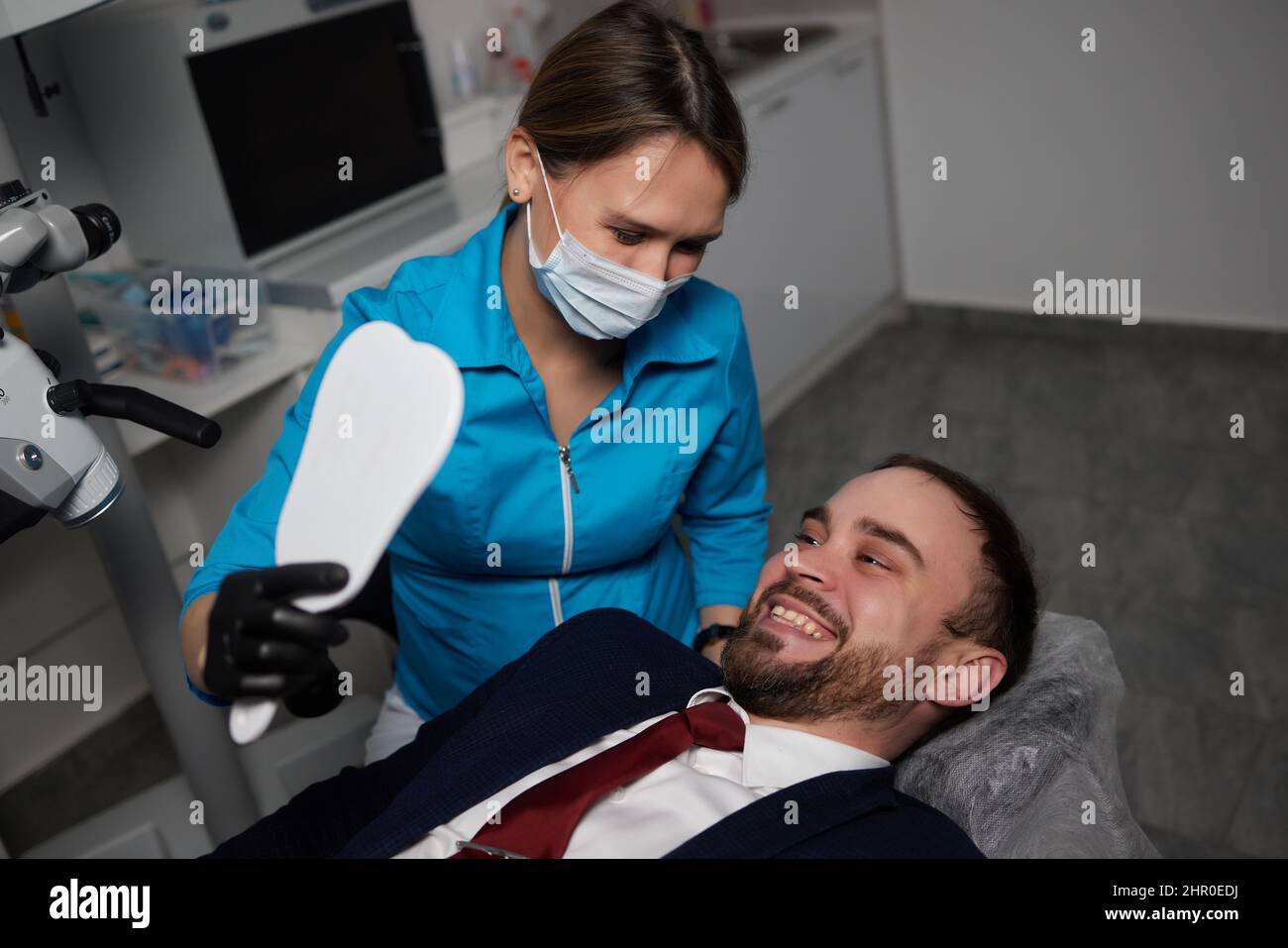 Smiling young man sitting in dentist chair while doctor examining his ...