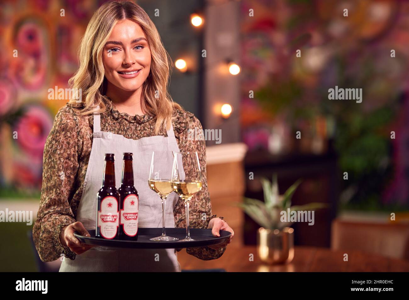 Portrait Of Smiling Female Server Holding Tray Of Drinks In Cool Bar Or ...