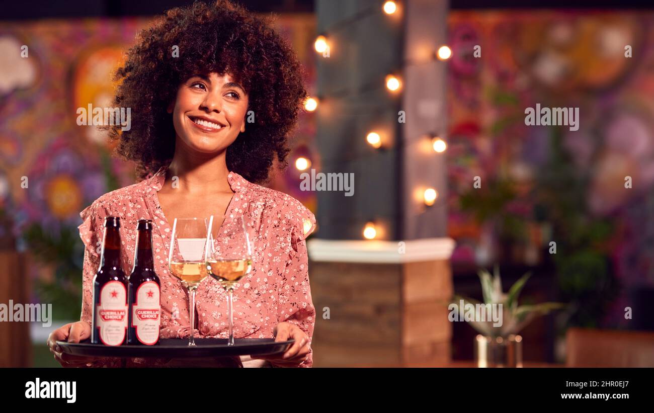 Portrait Of Smiling Female Server Holding Tray Of Drinks In Cool Bar Or ...