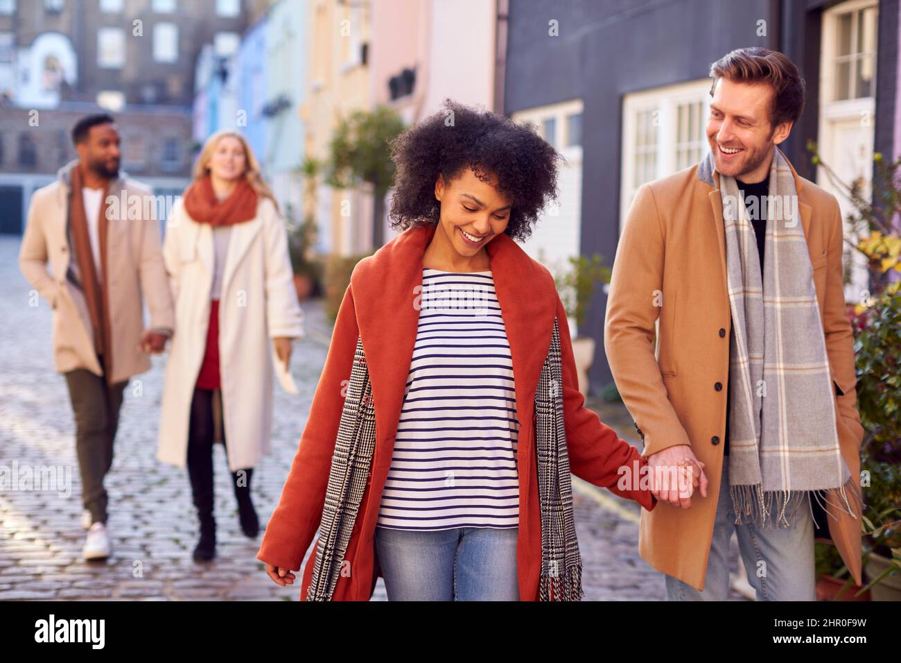 Multi Cultural Couple With Friends Walking Along Residential City ...