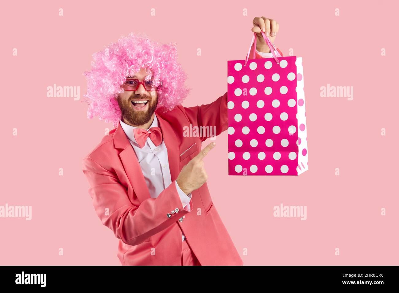 Funny clown in pink suit, wig and glasses showing paper shopping bag ...