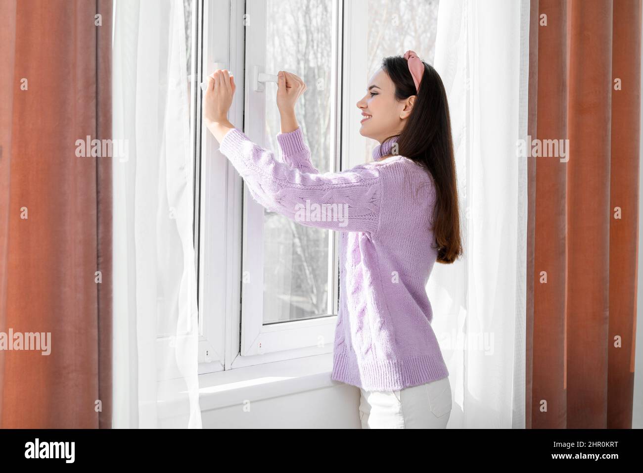 Pretty young woman opening window in room Stock Photo - Alamy