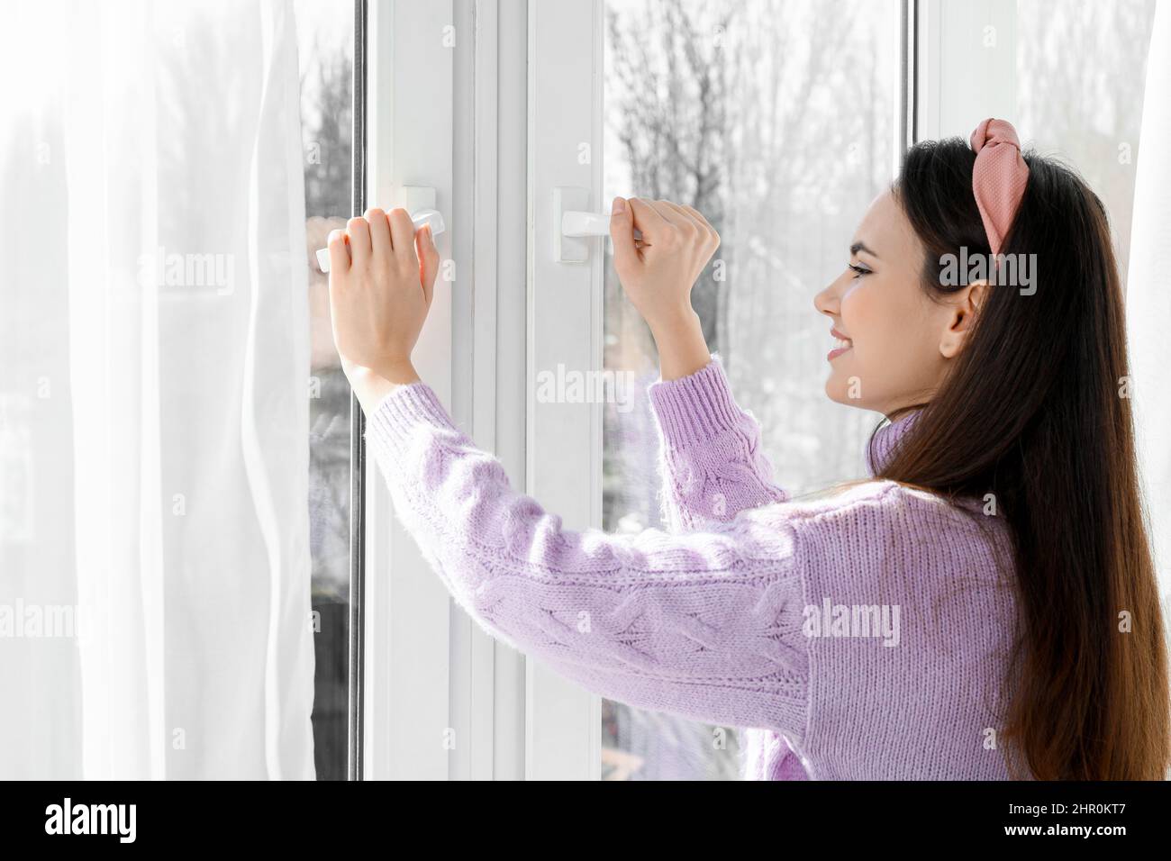Pretty young woman opening window in room Stock Photo - Alamy