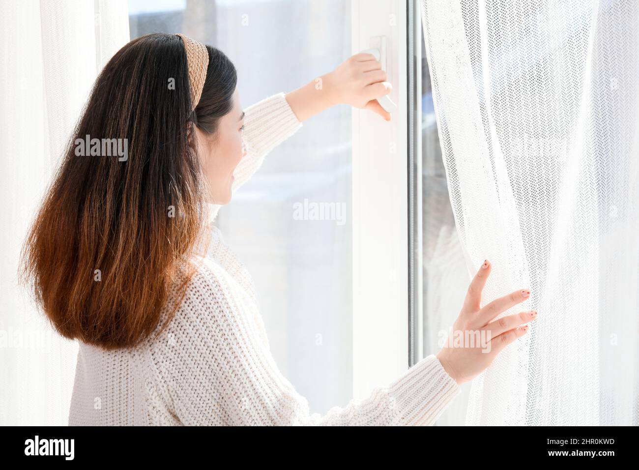 Pretty young Asian woman opening window at home Stock Photo - Alamy