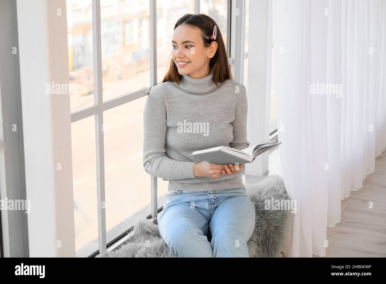 Pretty young woman reading book while sitting on window sill Stock ...