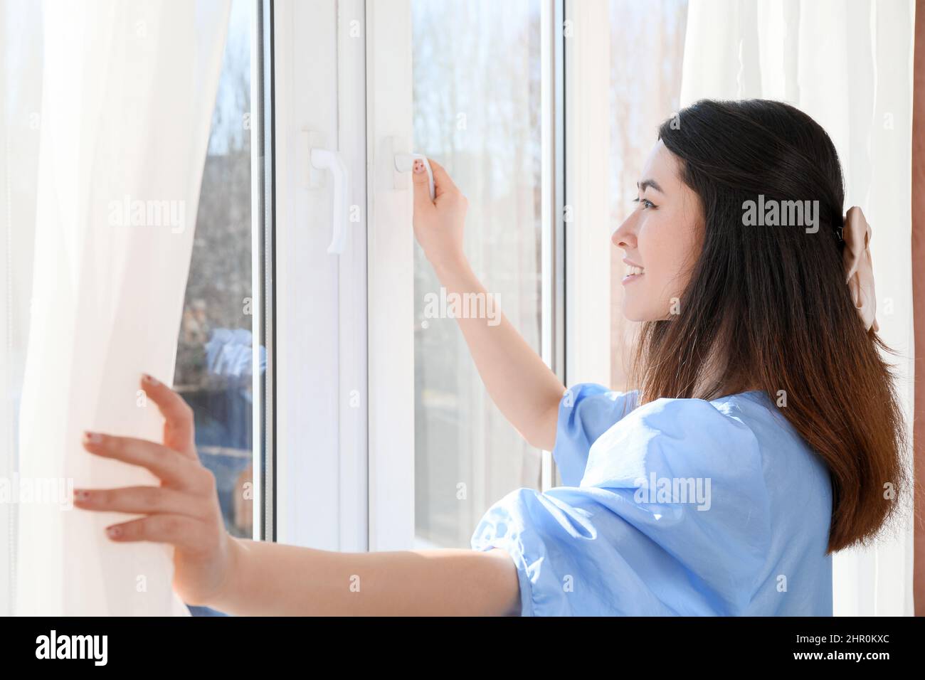 Pretty young Asian woman opening window in room Stock Photo - Alamy