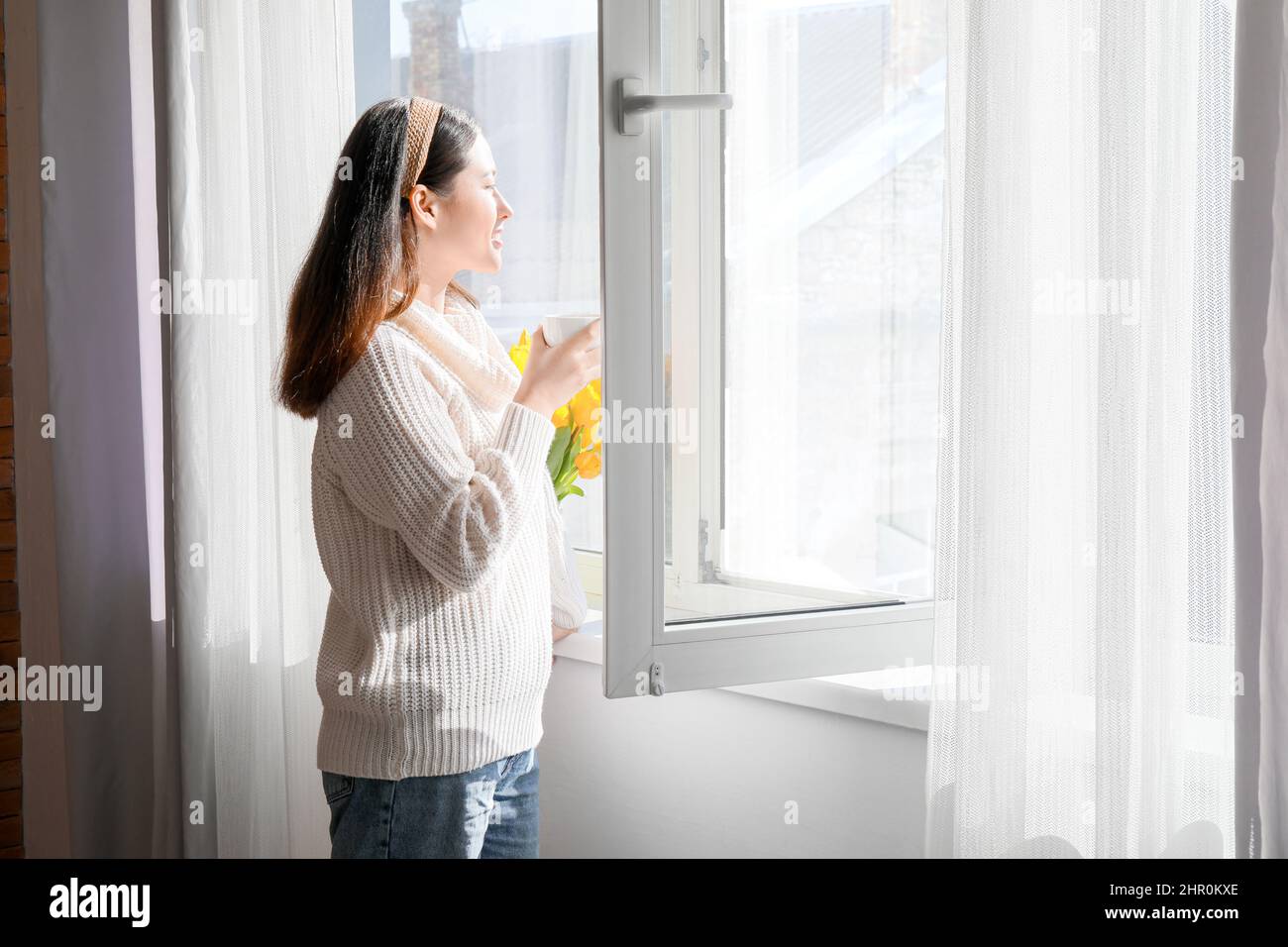 Pretty young Asian woman drinking tea near window Stock Photo - Alamy