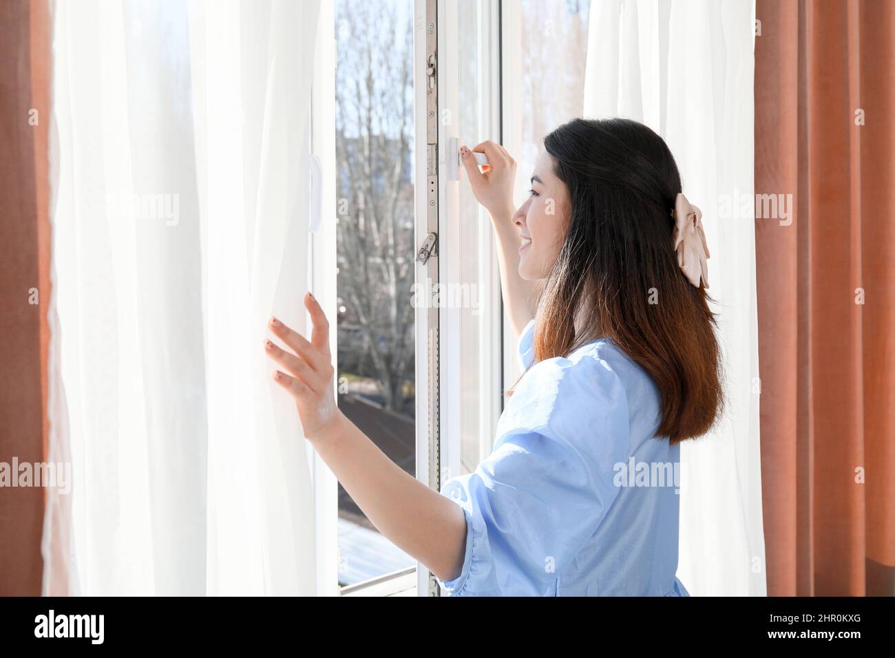 Pretty young Asian woman opening window in room Stock Photo - Alamy
