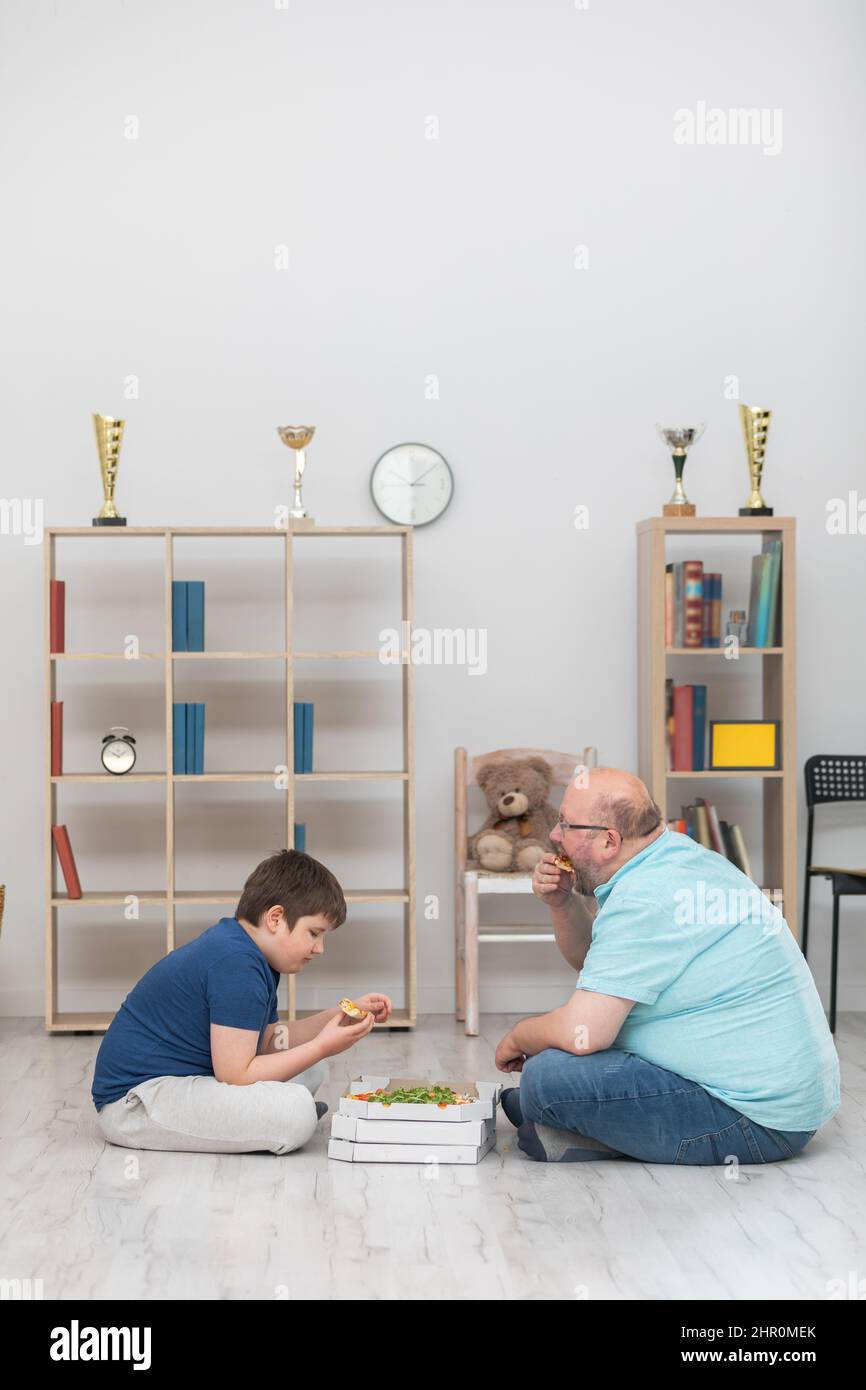 Dad and son are sitting on the floor eating fresh pizza Stock Photo - Alamy