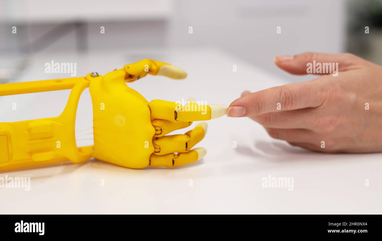 Woman's hand and a plastic hand prosthesis for a child on a white ...