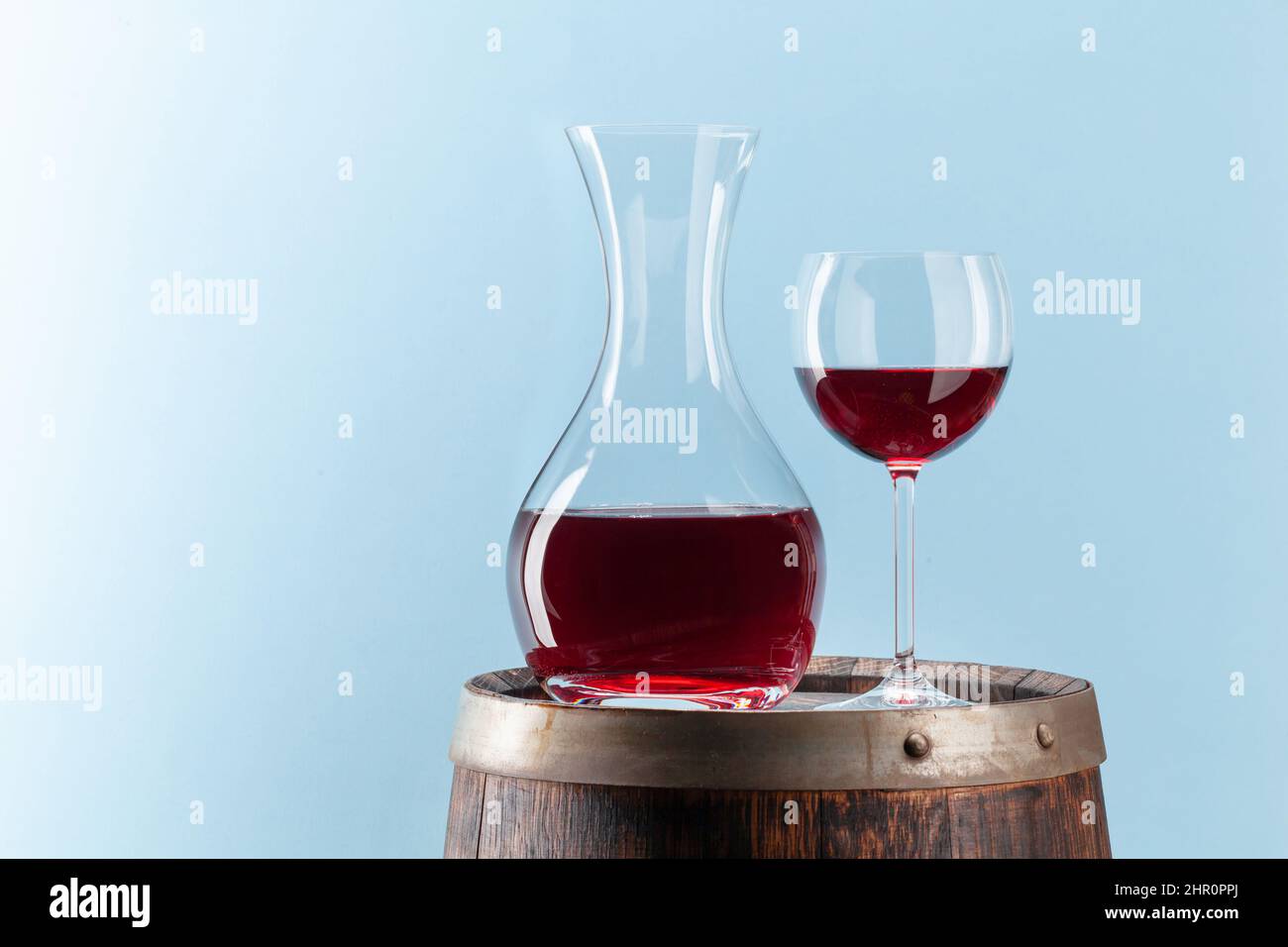 Decanter with red wine on old wooden barrel in front of blue background ...