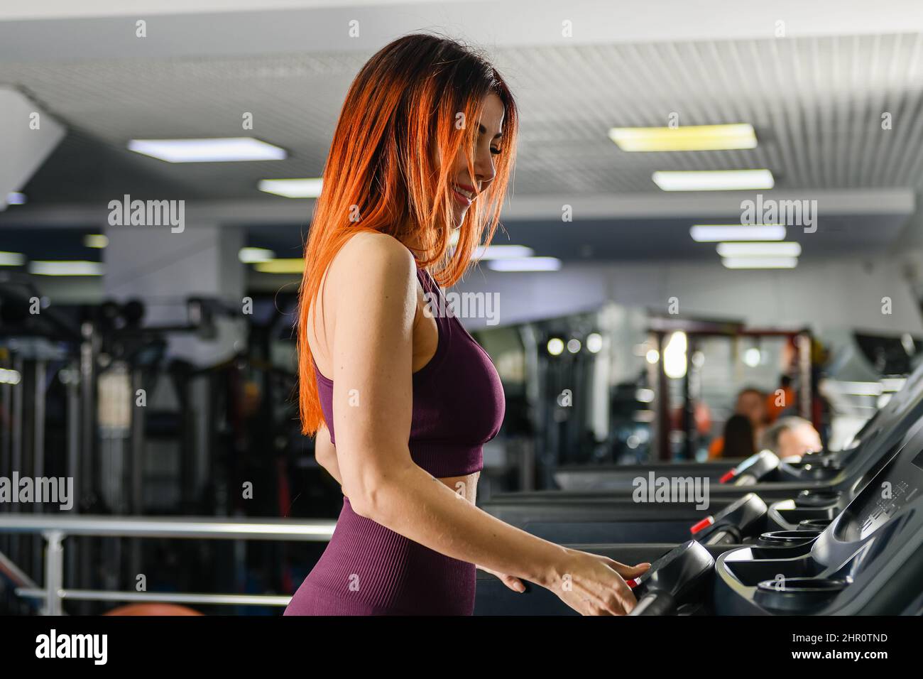 Fit woman with red hair press buttons and exercise at treadmill running ...