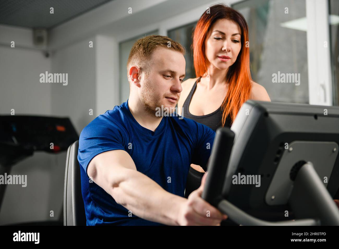 Female trainer teach man to use equipment machines at modern gym, look ...