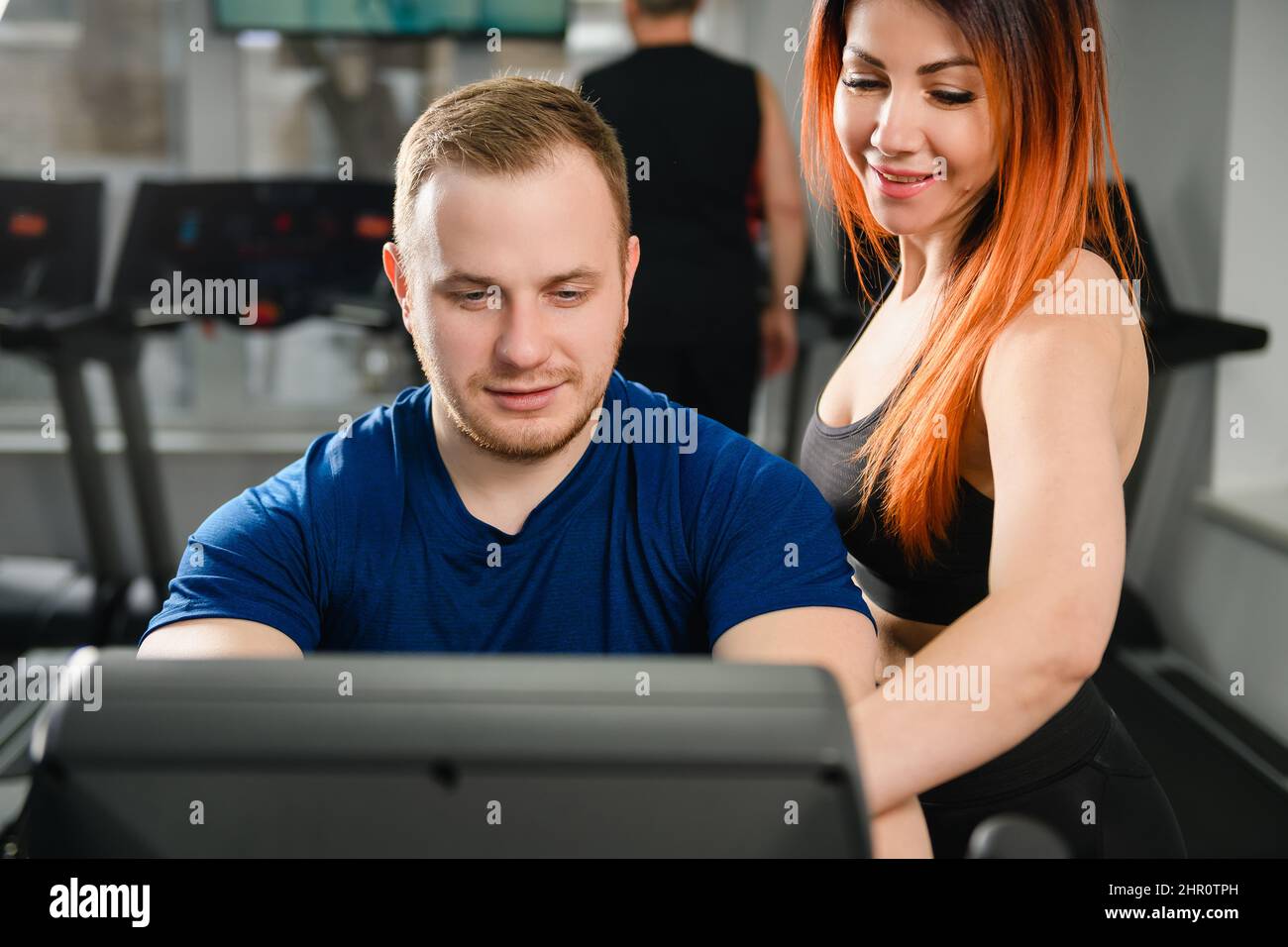 Trainer teach woman to use equipment machines at modern gym, look at ...