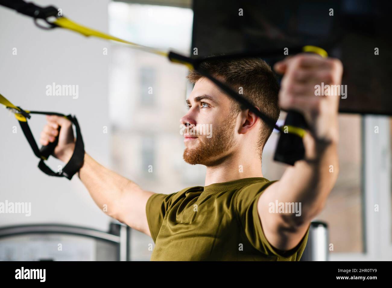 Portrait of young sportive man with beard exercise hands muscles at gym ...