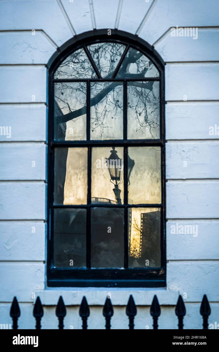 Reflection of a street lantern and tree at dusk in window of posh house ...
