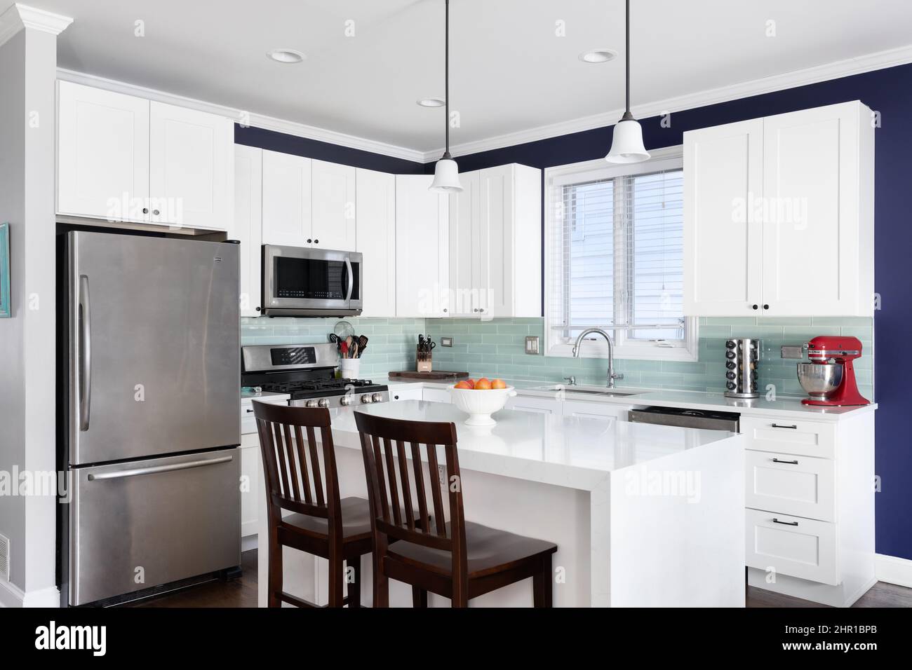 A kitchen with white cabinets and island, waterfall granite countertop ...