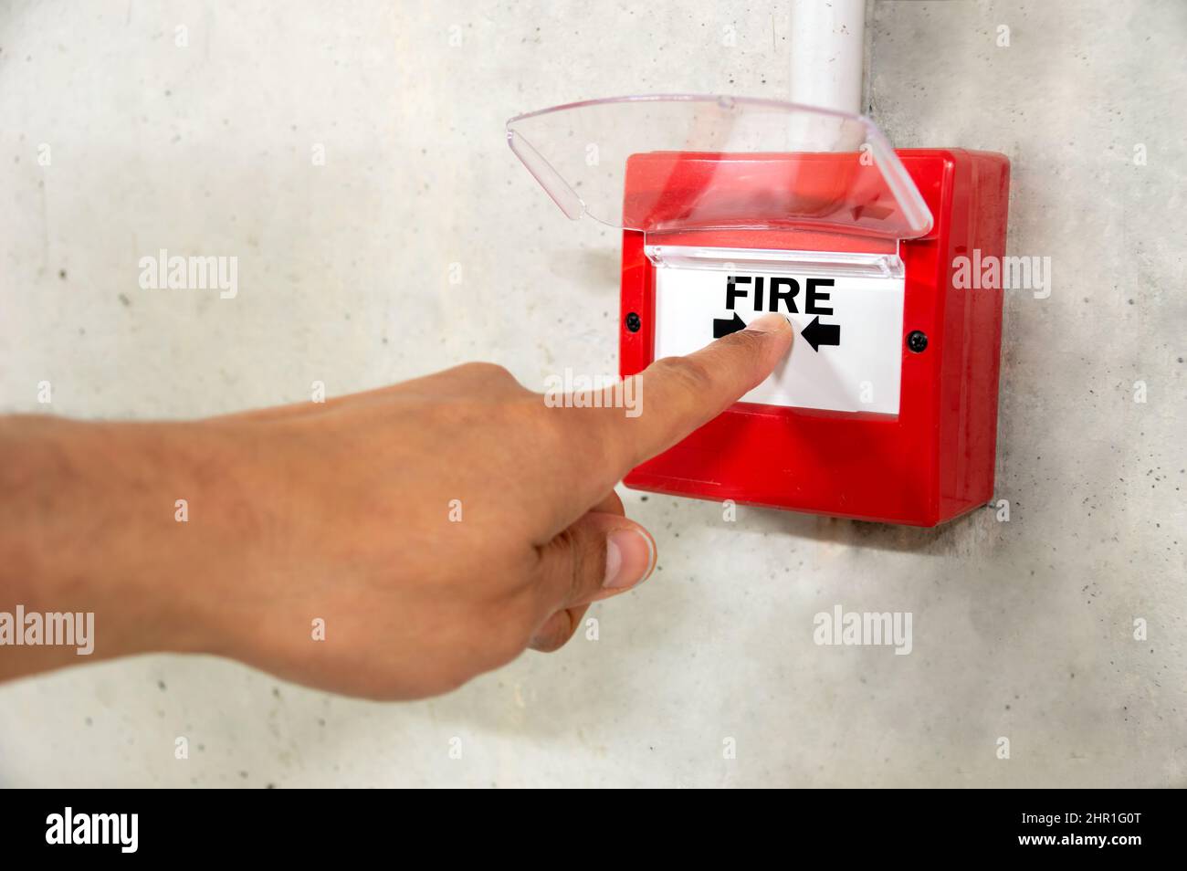 Close up of male hand pointing at red fire alarm switch on concrete ...