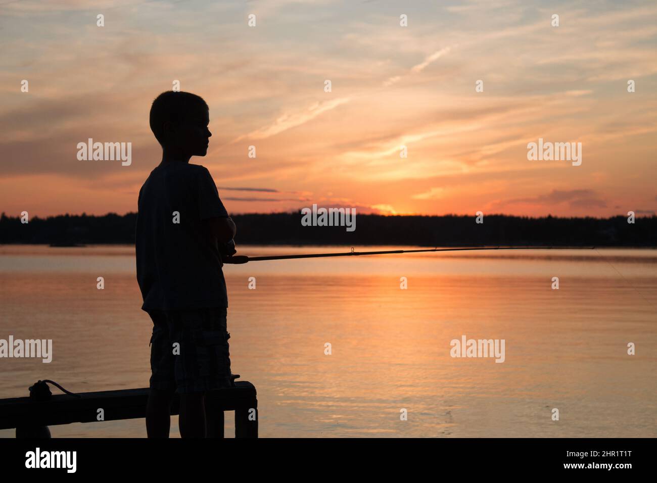 Boy fishing on a dock at sunset Stock Photo - Alamy