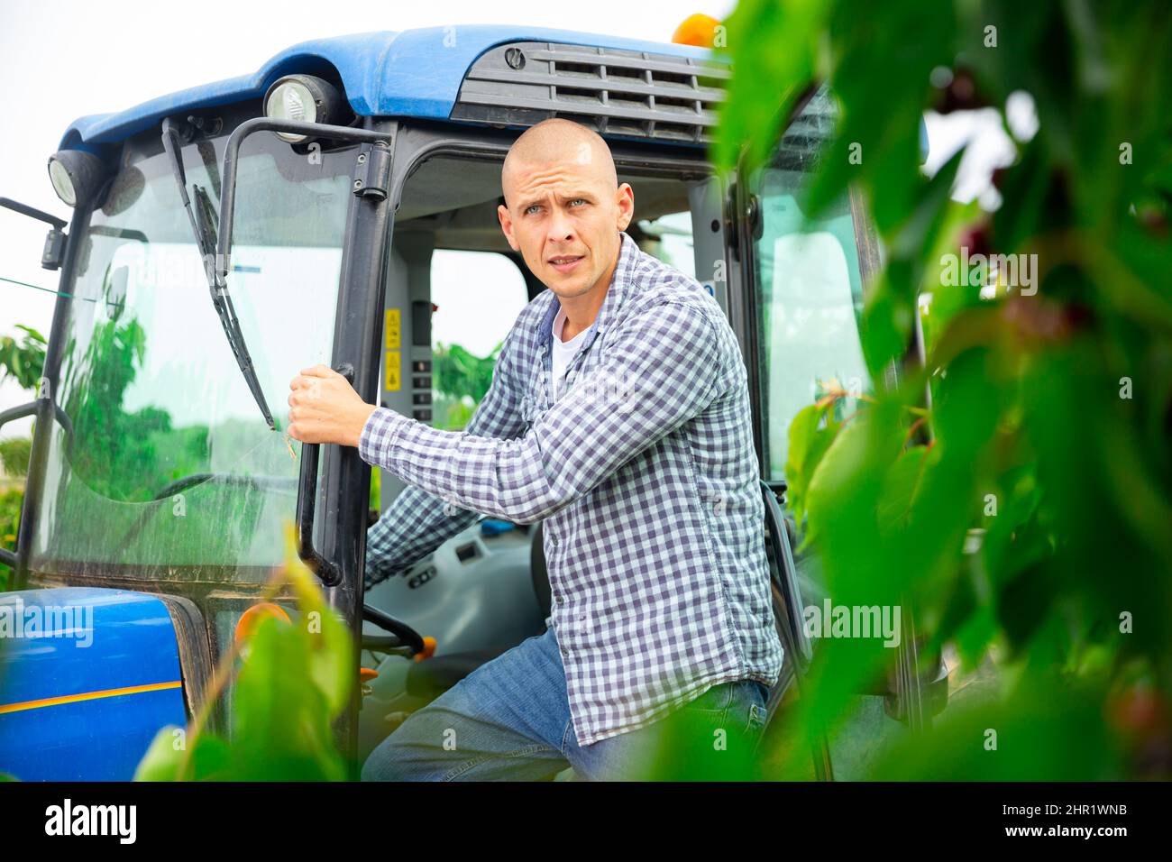 Skilled male farmer working on farm tractor in orchard Stock Photo - Alamy