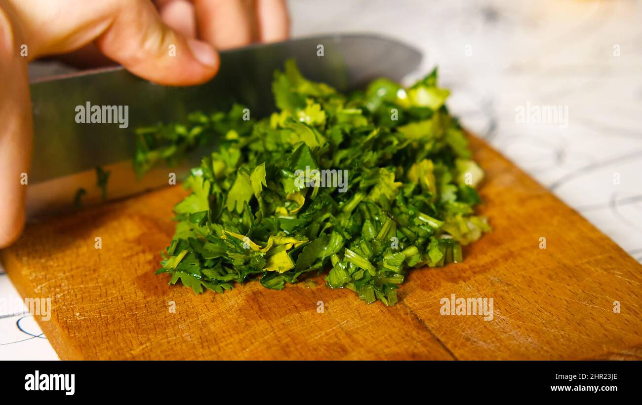 A close-up of a woman's hand with a knife is chopping parsley on a ...
