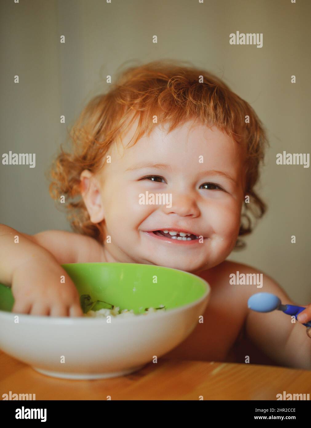 Launching child eat. Happy baby eating himself with a spoon. Smiling ...