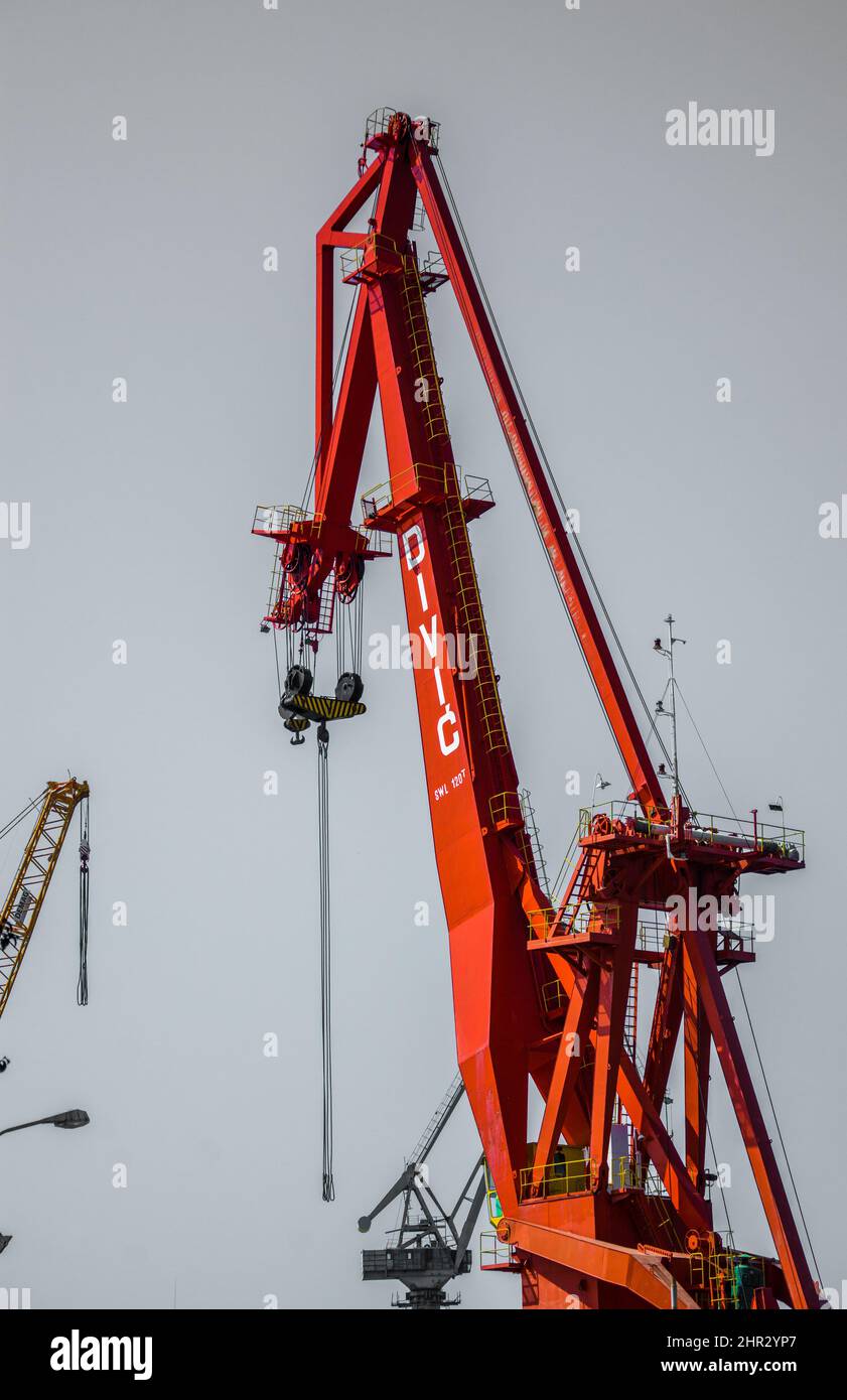Vertical closeup of a red harbor crane during loading against a gray ...