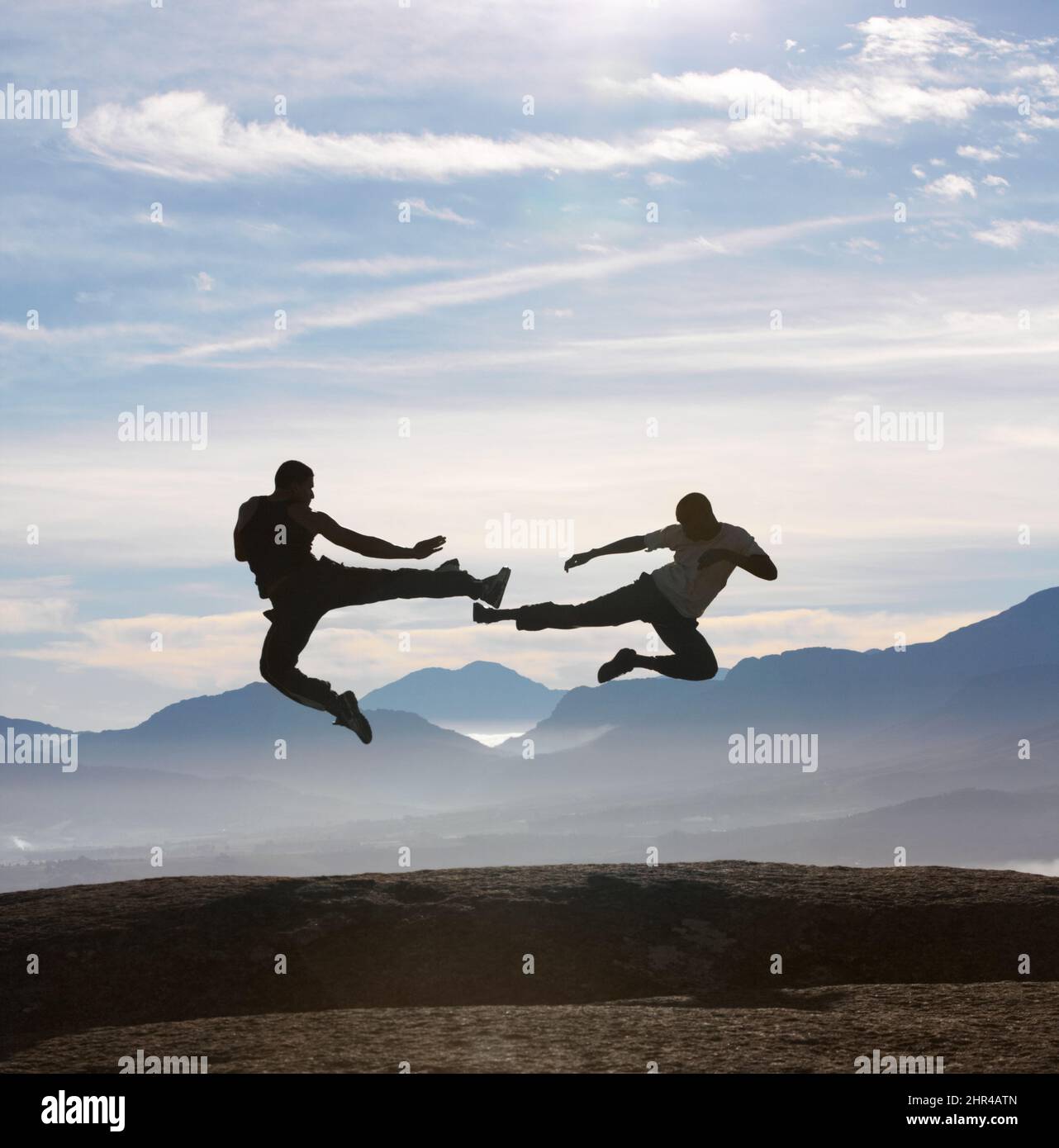 Flying feet on a mountain. Two male kickboxers fly kicking one another ...