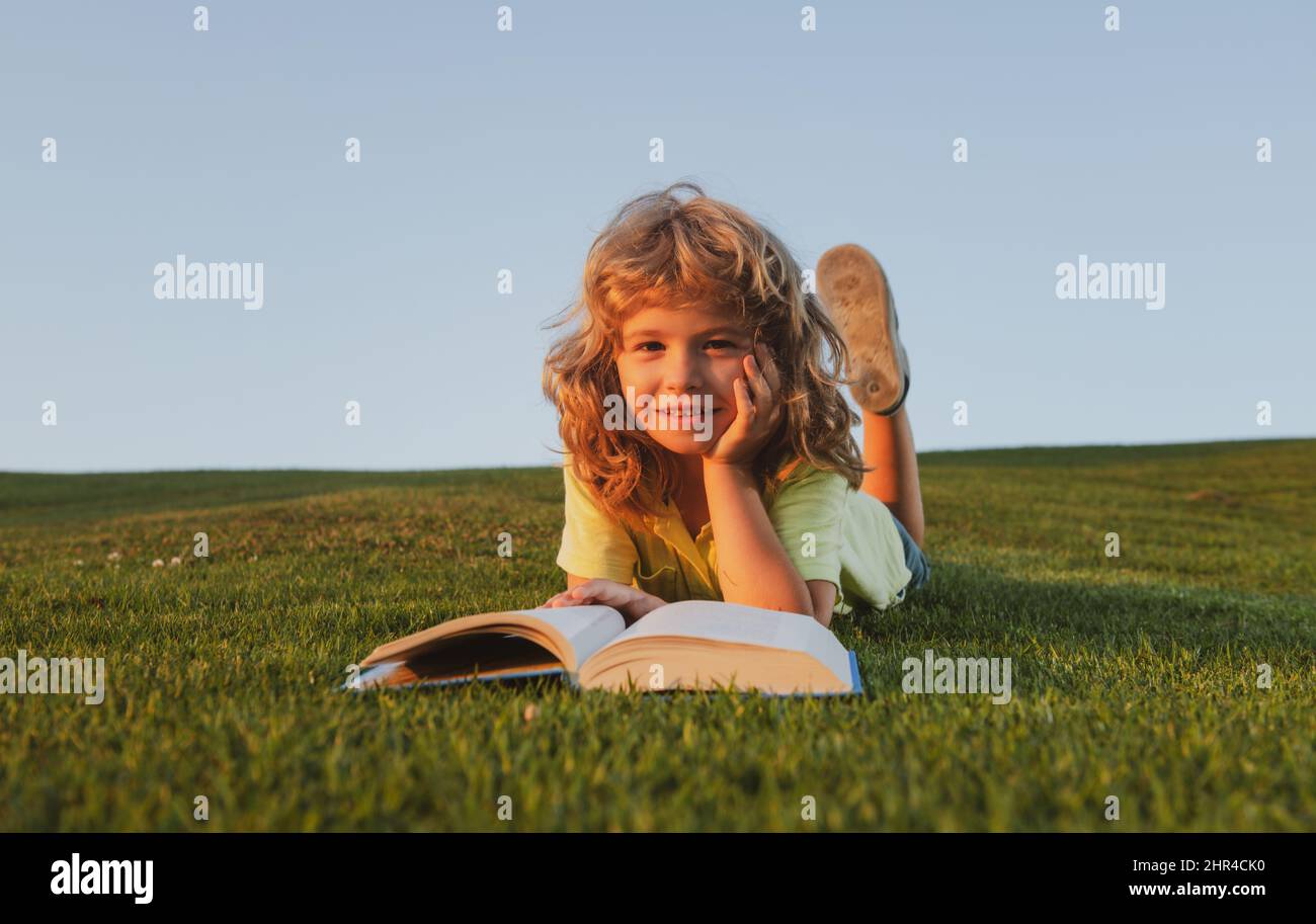Clever child boy reading book laying on grass on grass and sky ...