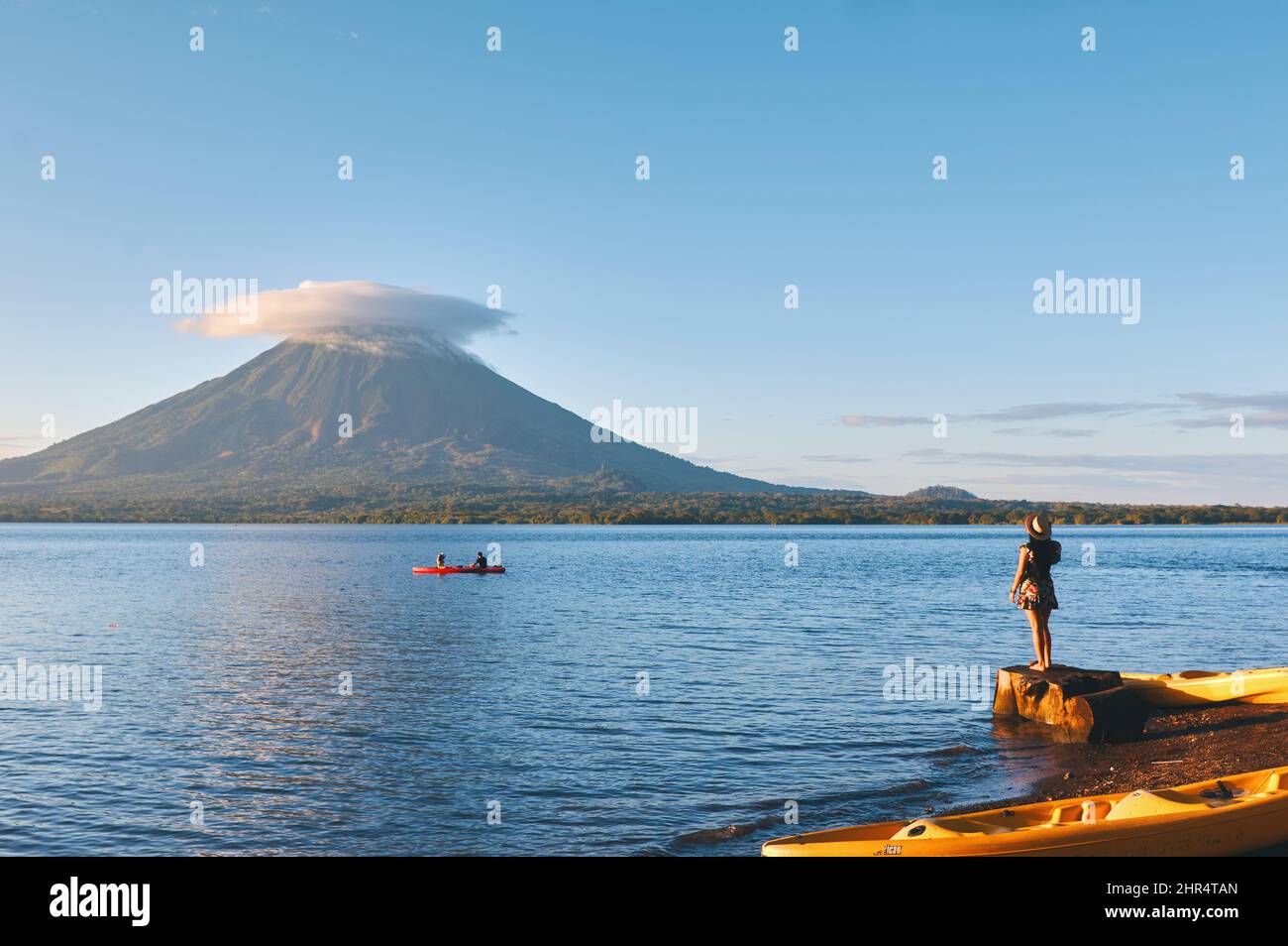 Young Hispanic female in a hat standing on the shore of a lake with a ...